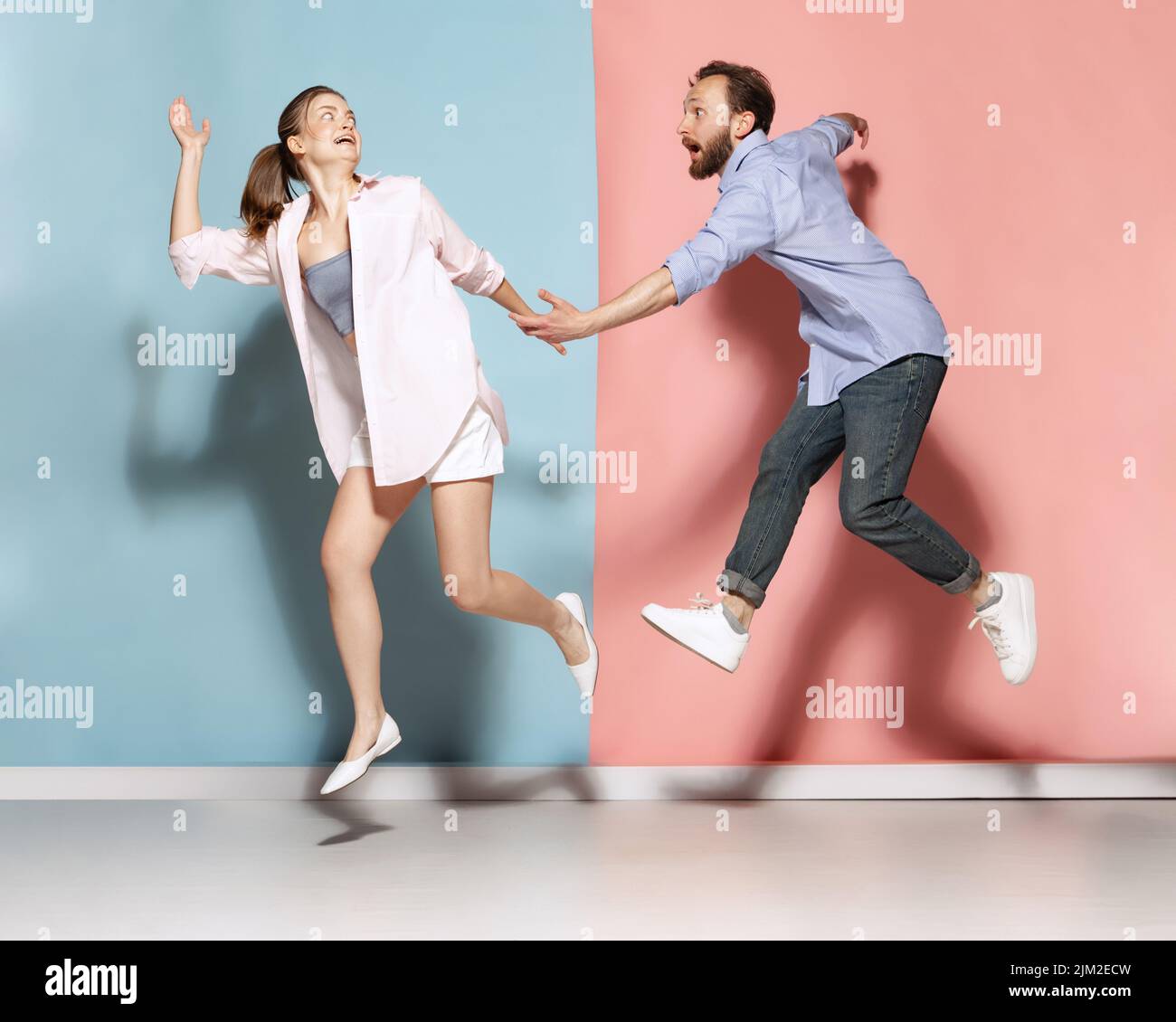 Astonished man and woman running, jumping isolated over blue and pink ...