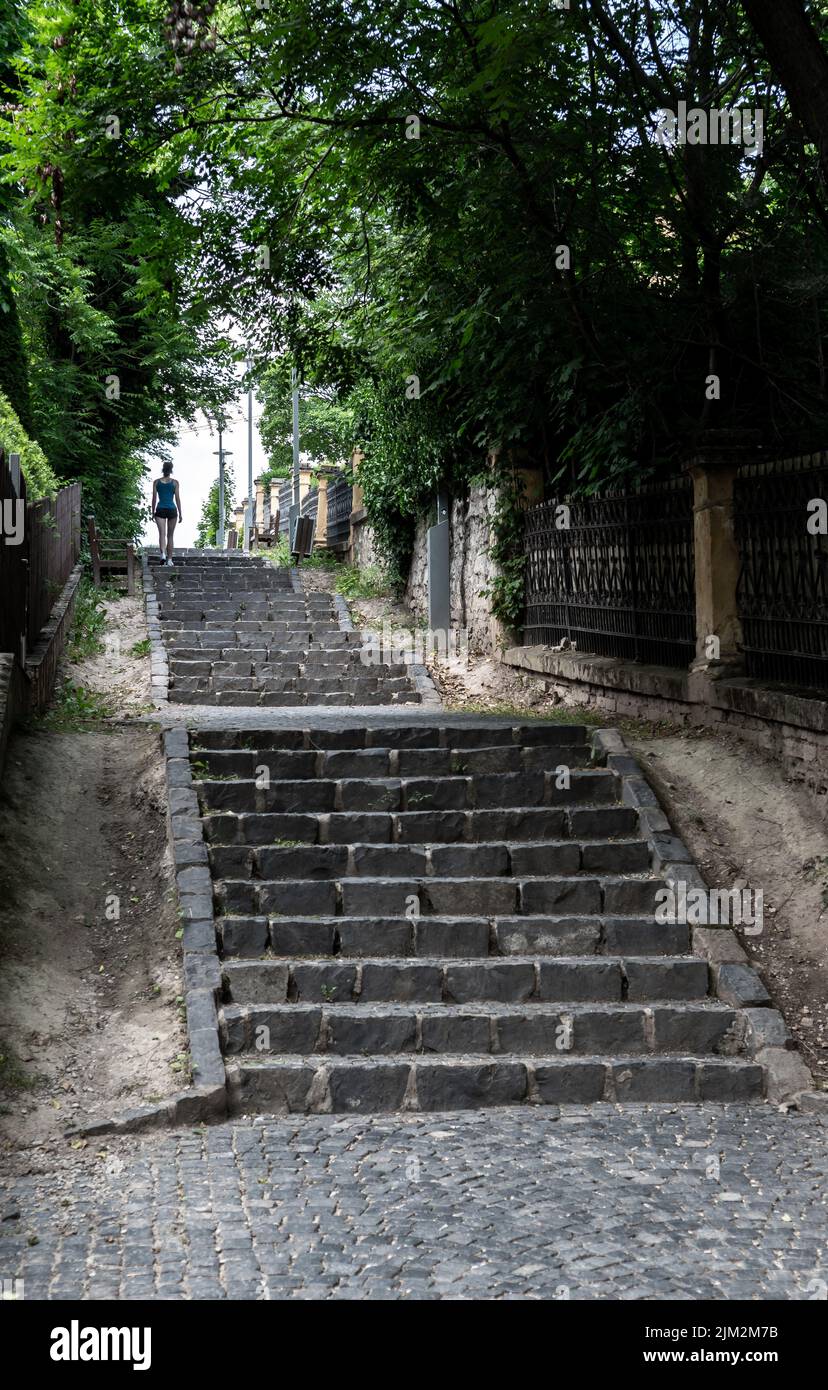 Young sporty woman in sportswear running up steep cobblestone stairs in ...