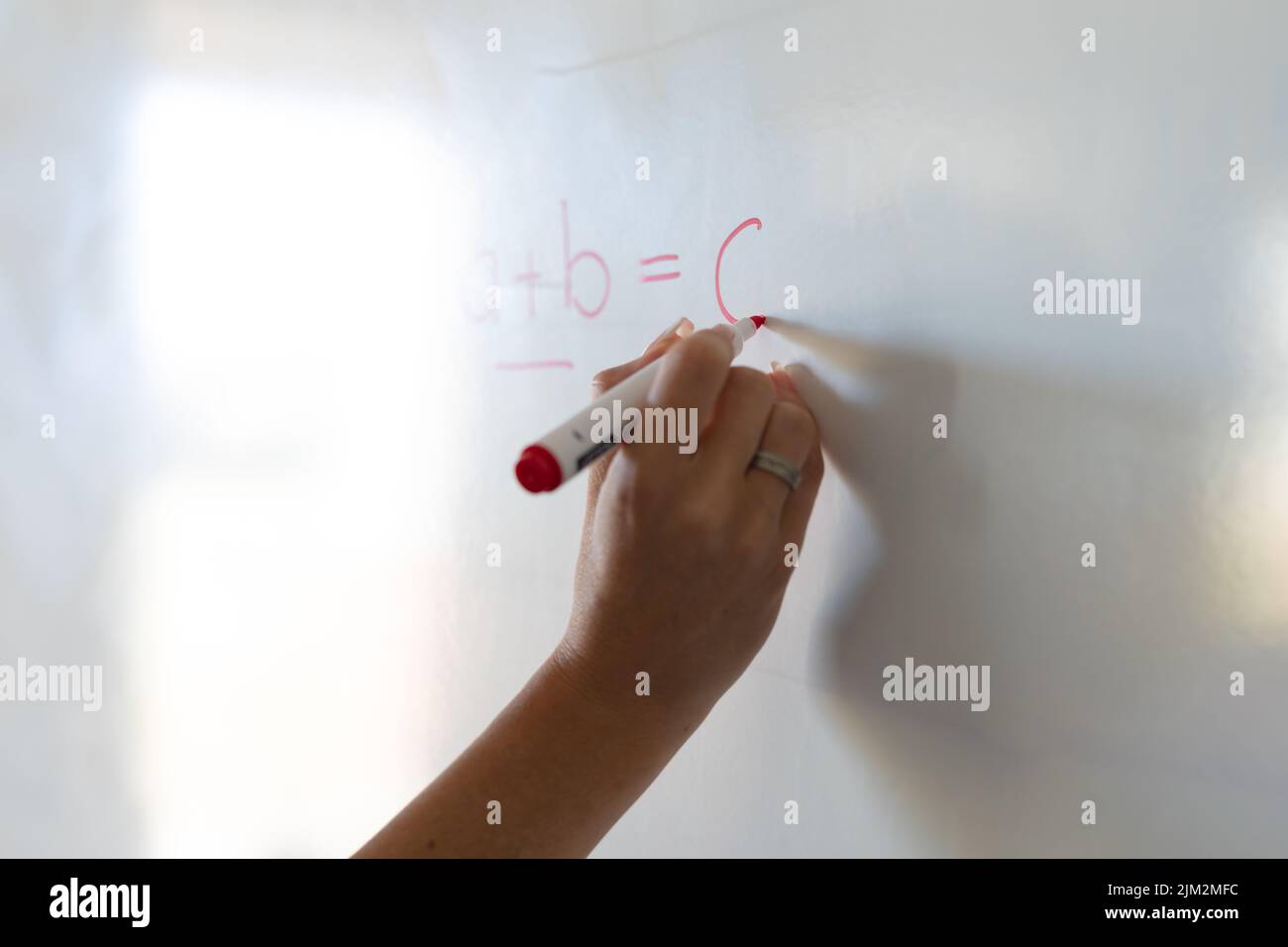 Cropped hand of caucasian female teacher writing formula on whiteboard ...