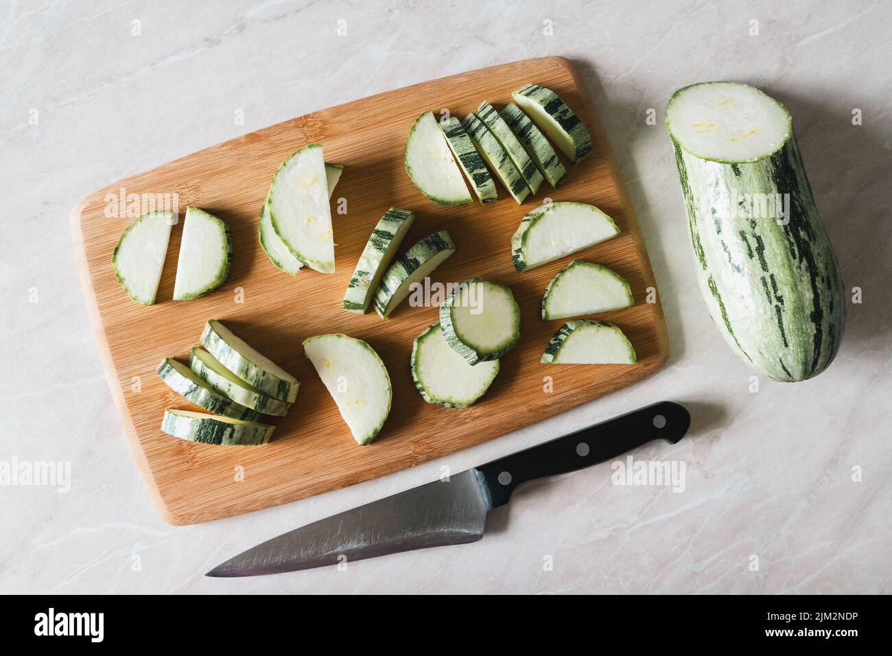 Zucchini cut into slices on cutting board, half squash, knife on white ...
