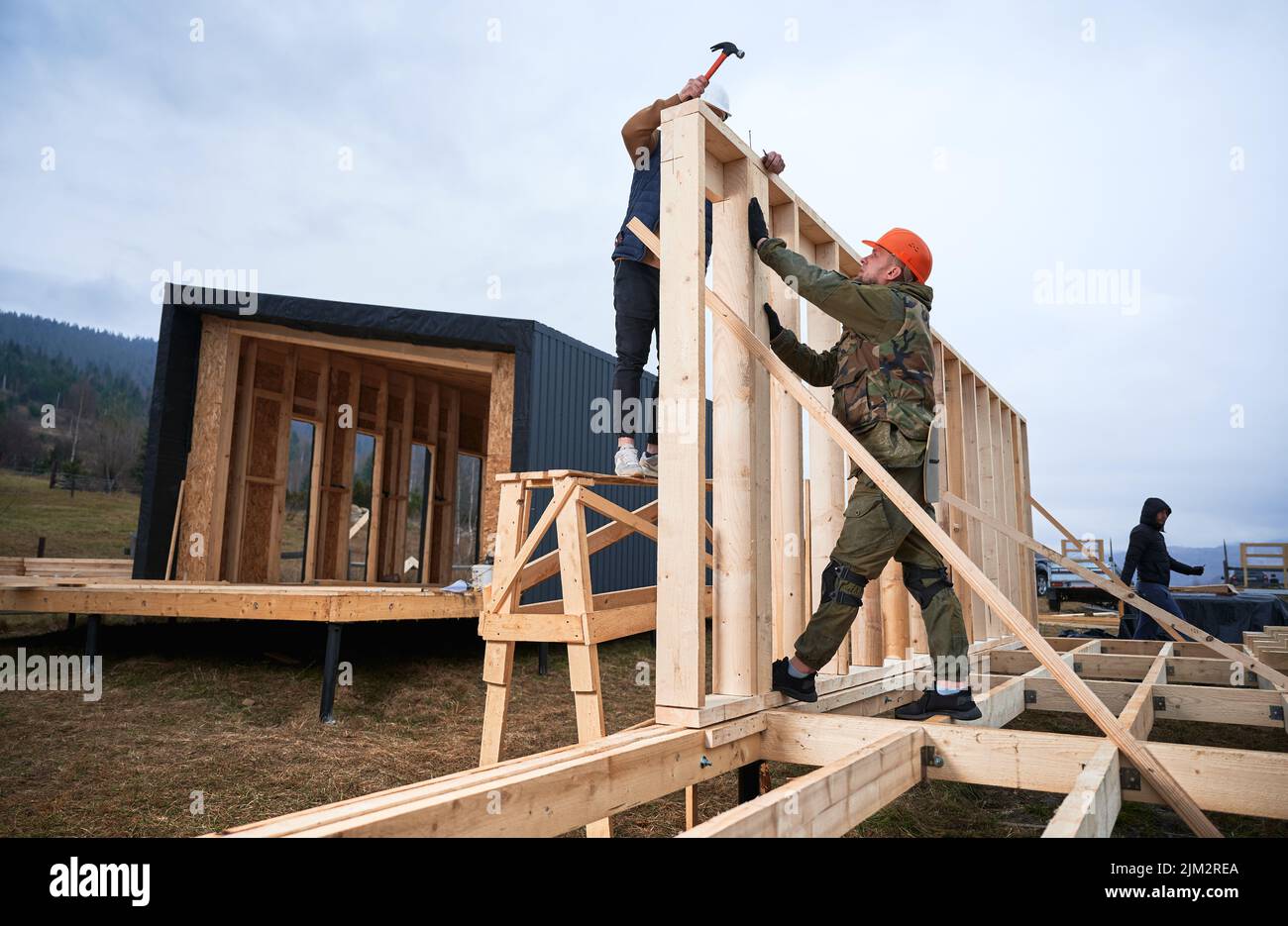 Man worker building wooden frame house on pile foundation. Carpenter ...