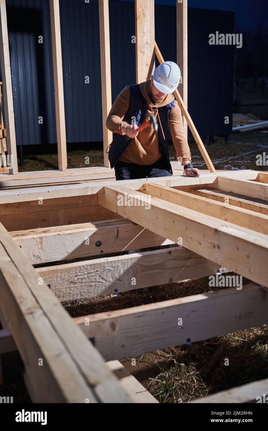 Man worker building wooden frame house on pile foundation. Carpenter ...