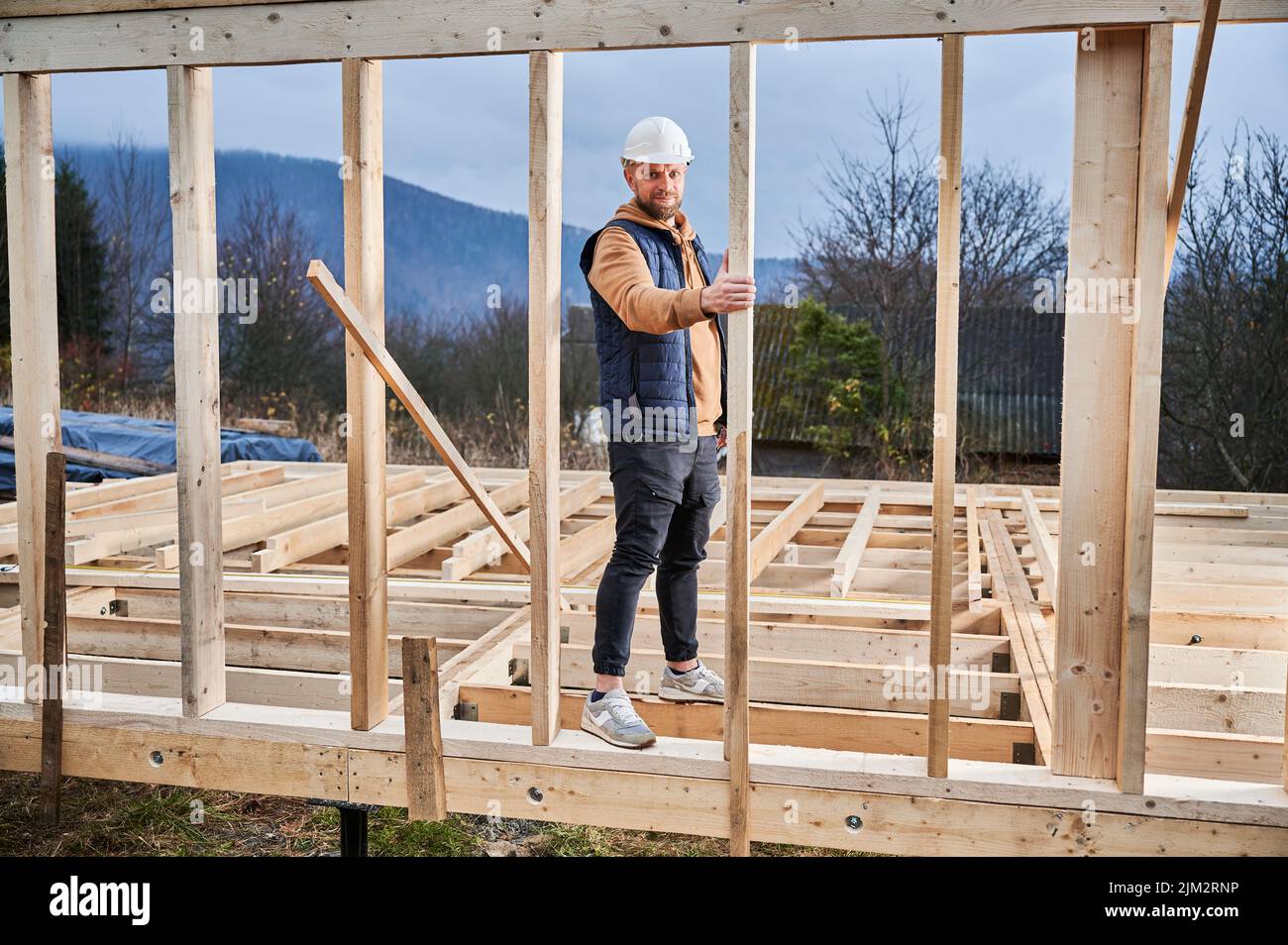 Male builder building wooden frame house. Portrait of man standing on construction site in ...