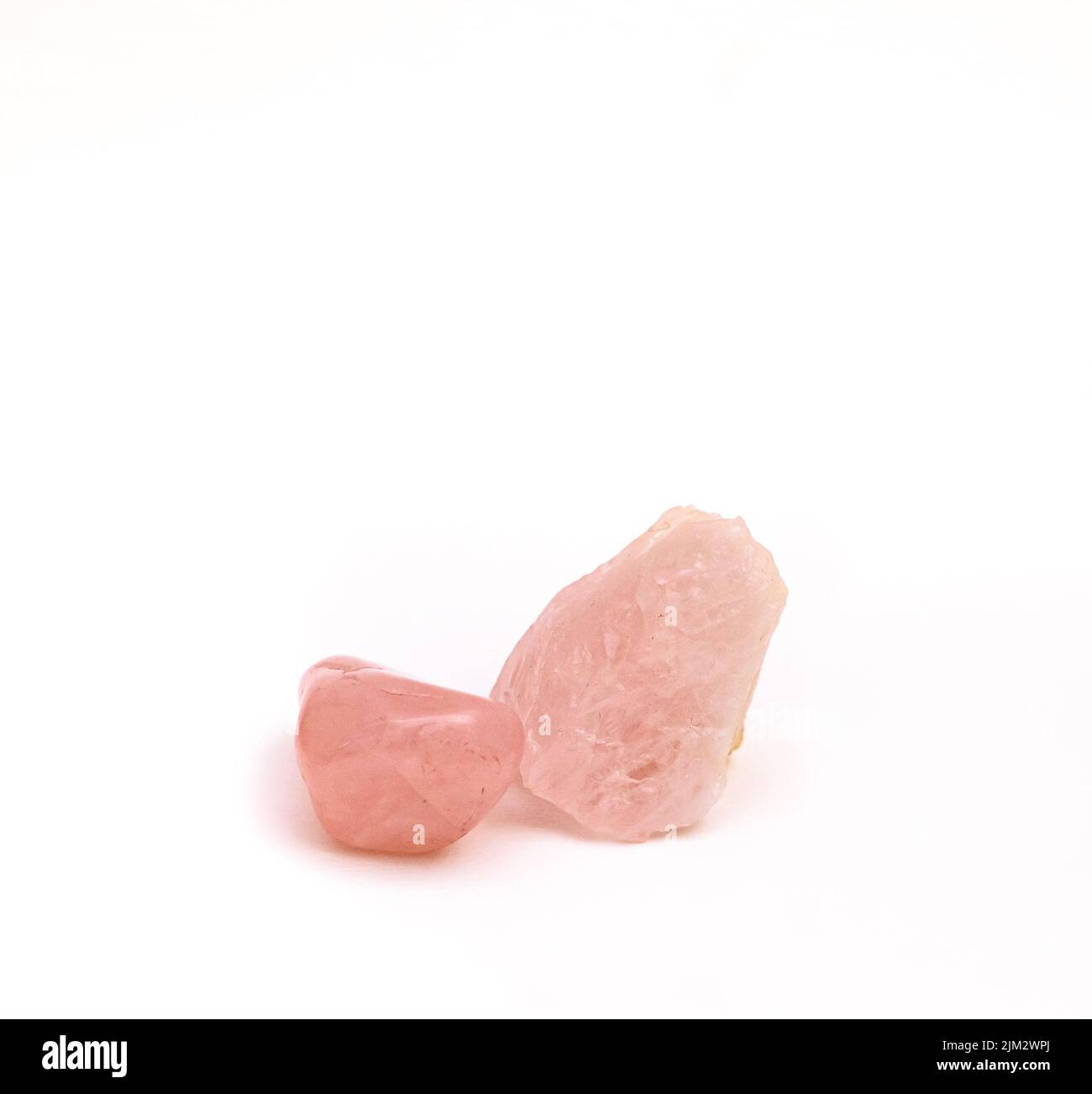 Polished rose quartz and raw/unpolished rose quartz crystal on a plain ...