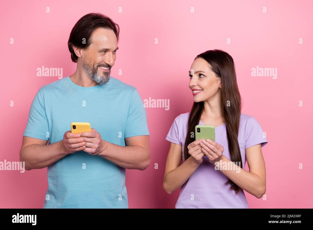 Photo of two positive idyllic people hold telephone look each other ...
