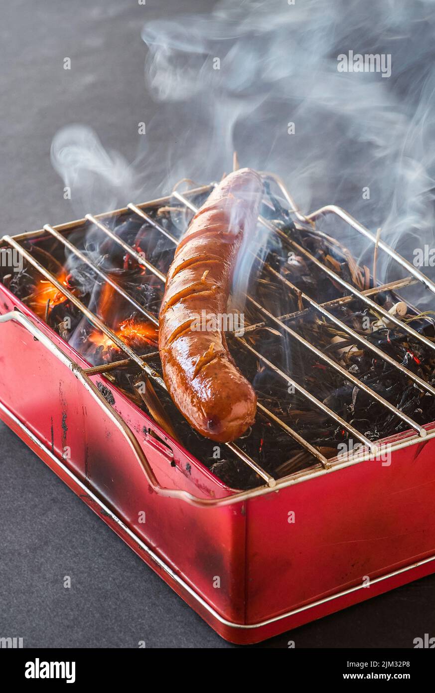 A fresh pork sausage grilling over an improvised barbecue on a metal ...