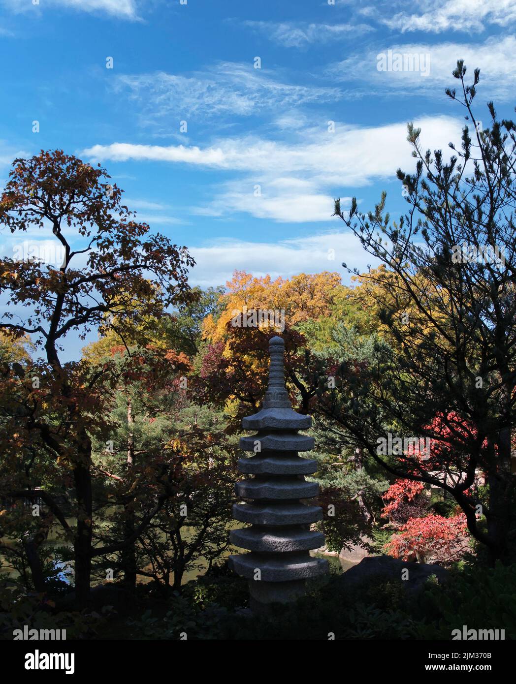 A Japanese Stone Pagoda stature nestled among a variety of trees with ...