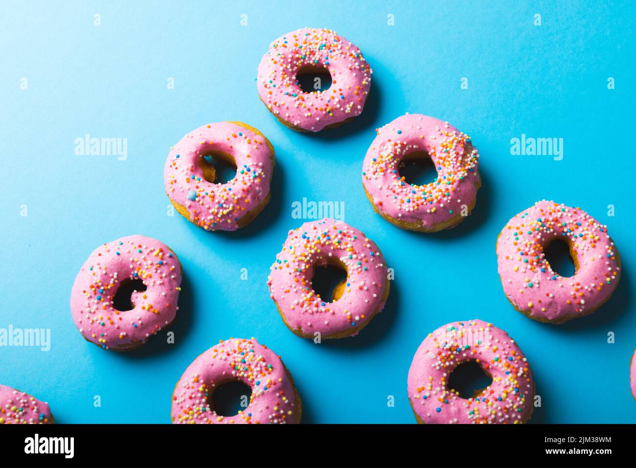 Overhead view of fresh donuts with sprinklers arranged against blue ...