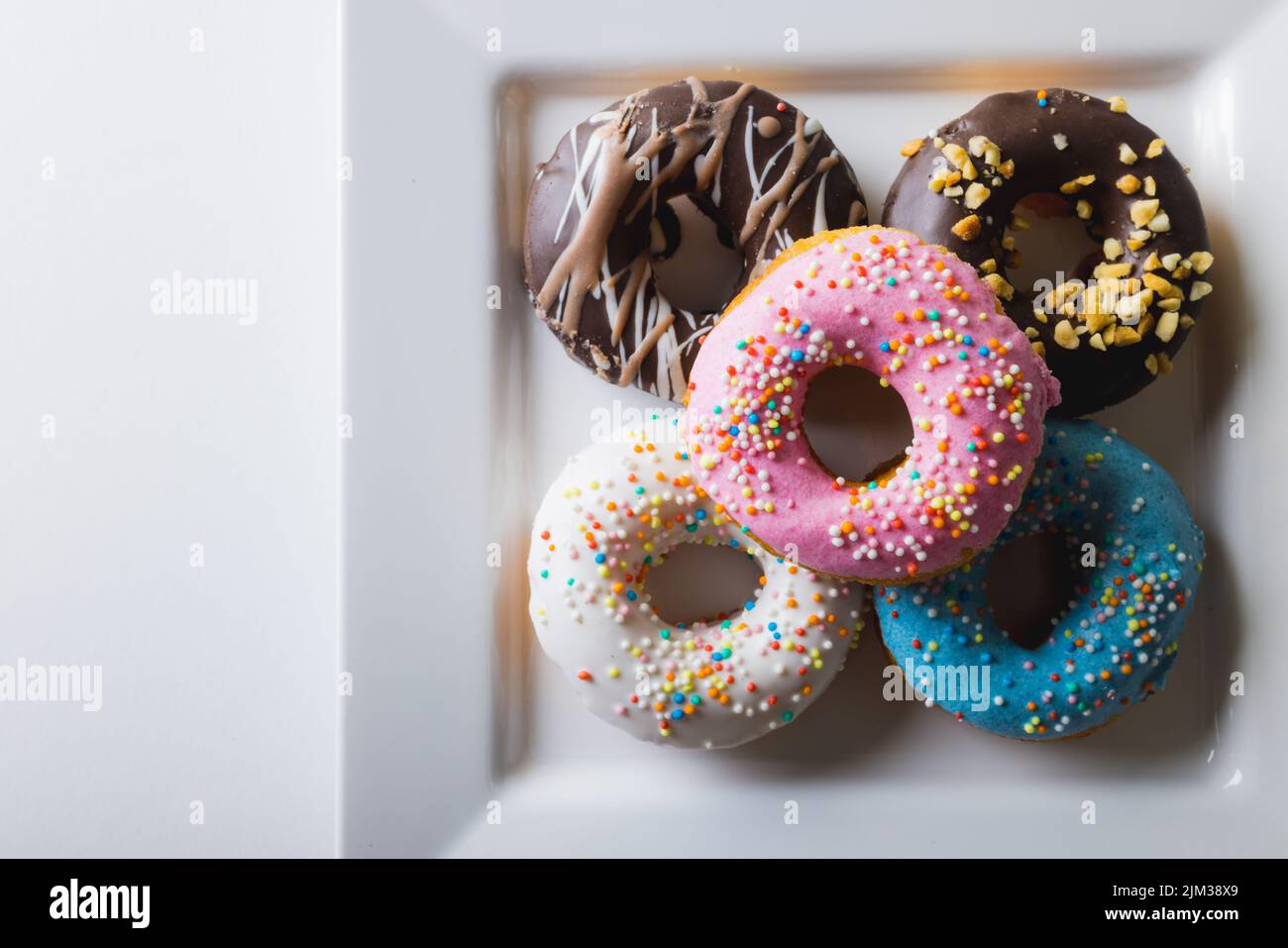 Overhead view of fresh multi colored donuts in plate over white ...