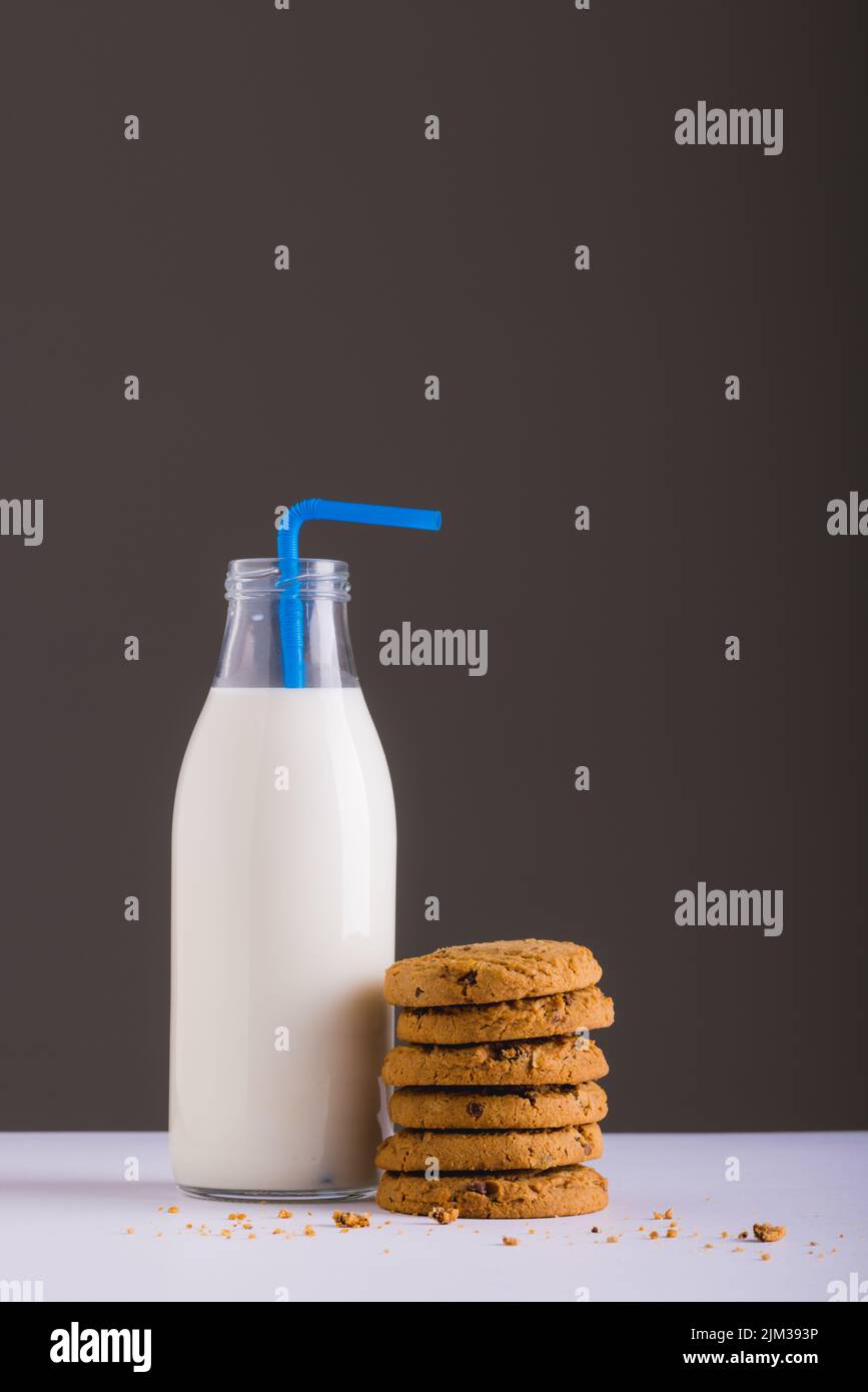 Milk bottle with straw by stack of cookies against gray background ...