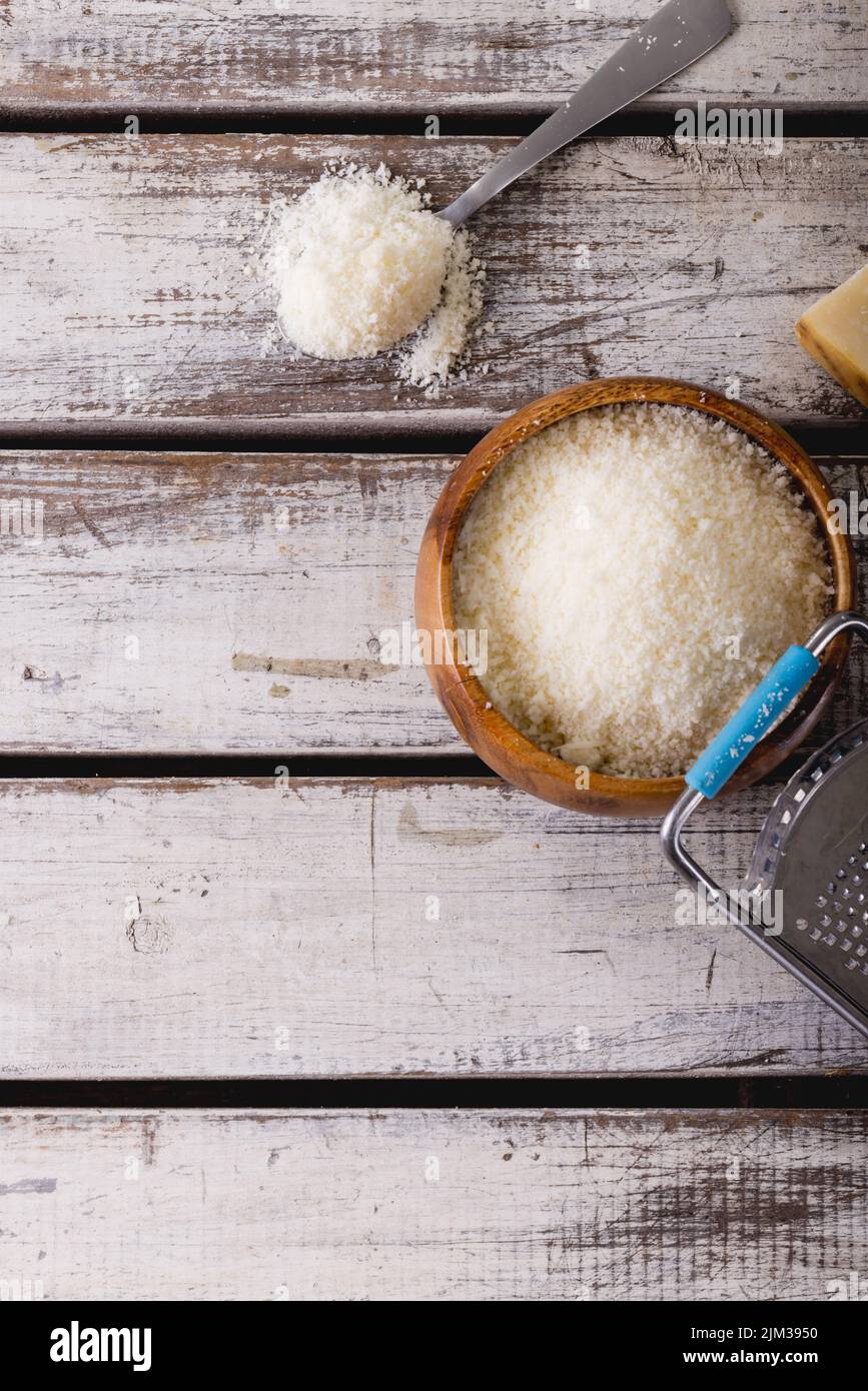 Overhead view of grated cheese with spoon and bowl on wooden table ...