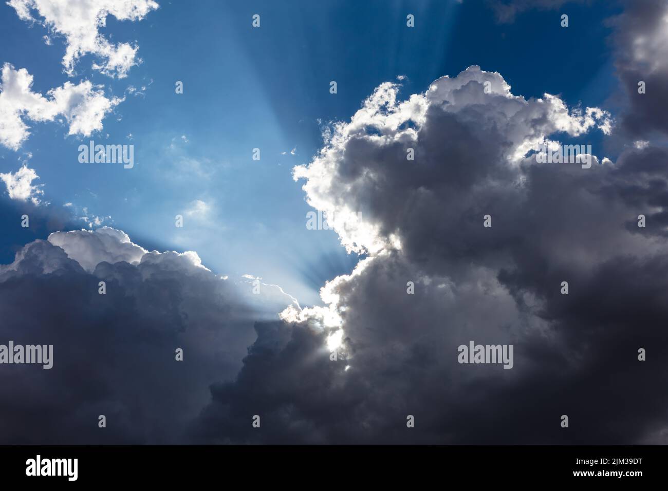 Closeup of cumulus clouds in blue sky. Rays of light emanating from sun ...