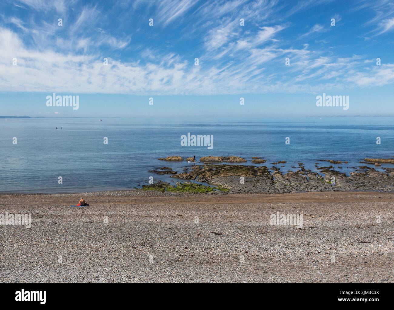 An isolated spot of beach with a sun bather and paddle boarder both ...