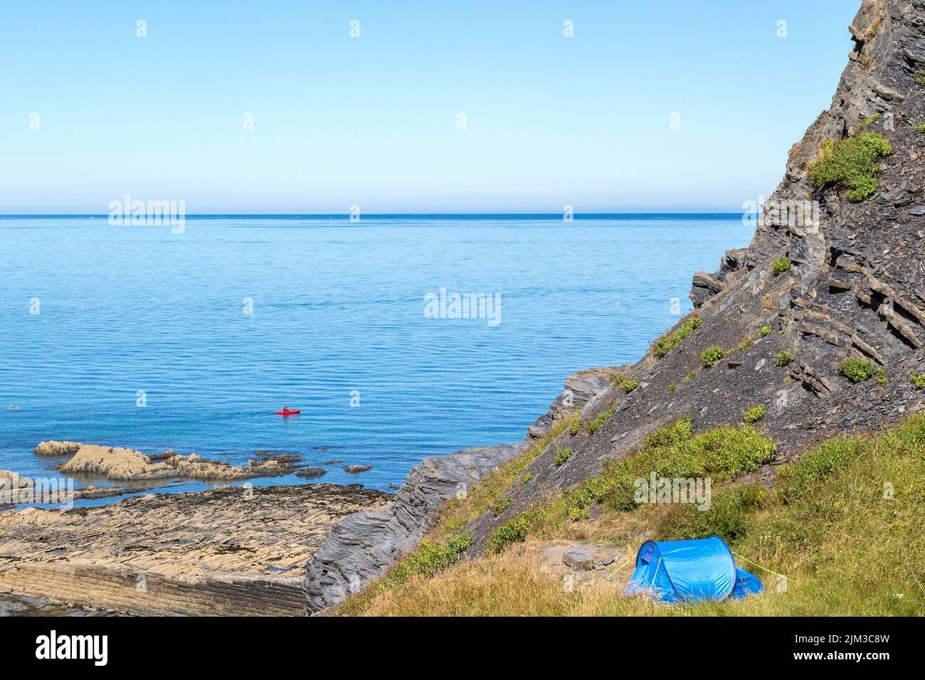 A tent is pitched on a large hill or mountain. Below in the sea a ...