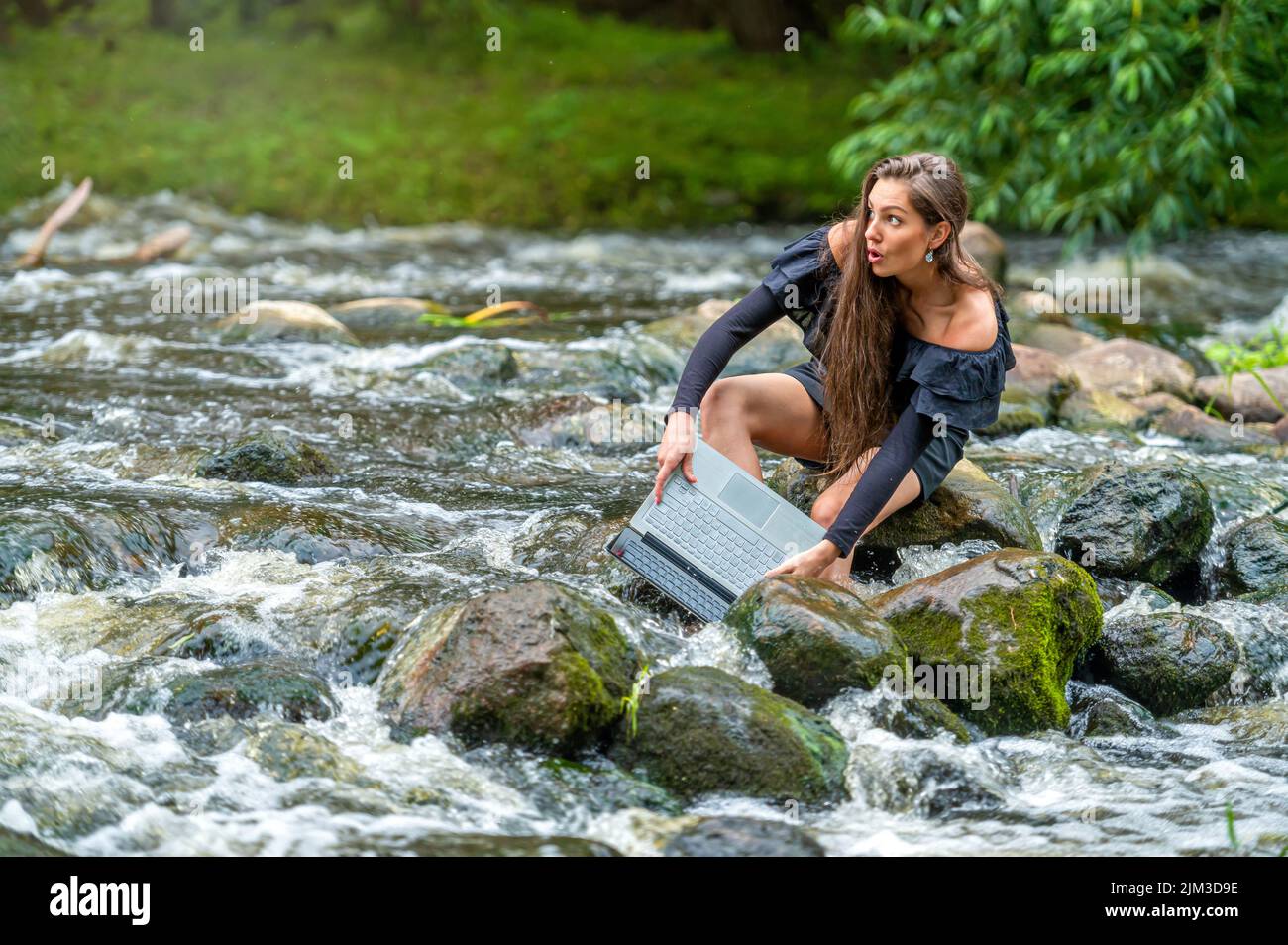 a woman uses a computer while sitting on a rock in the river,laptop ...