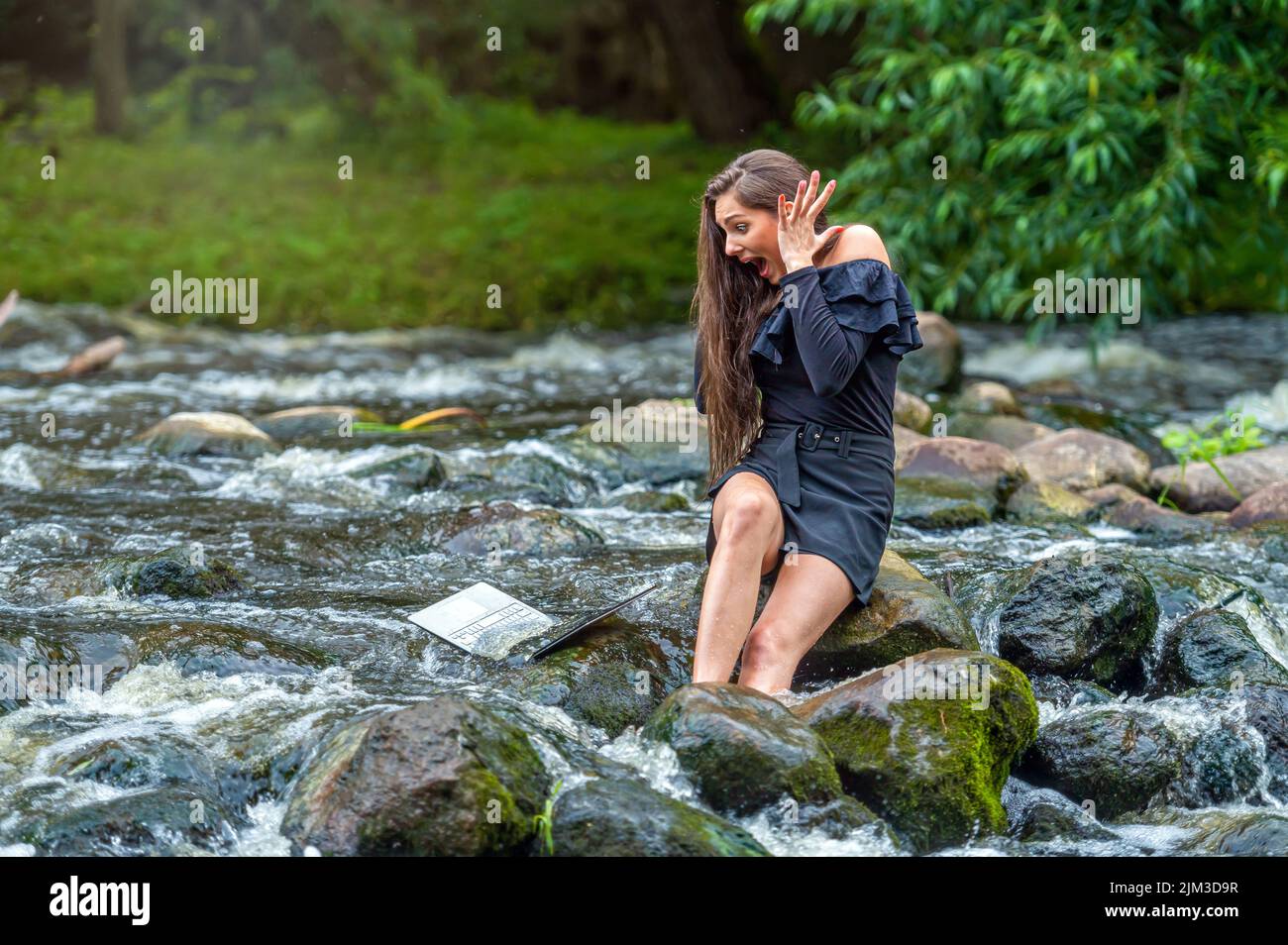 a woman uses a computer while sitting on a rock in the river,laptop ...