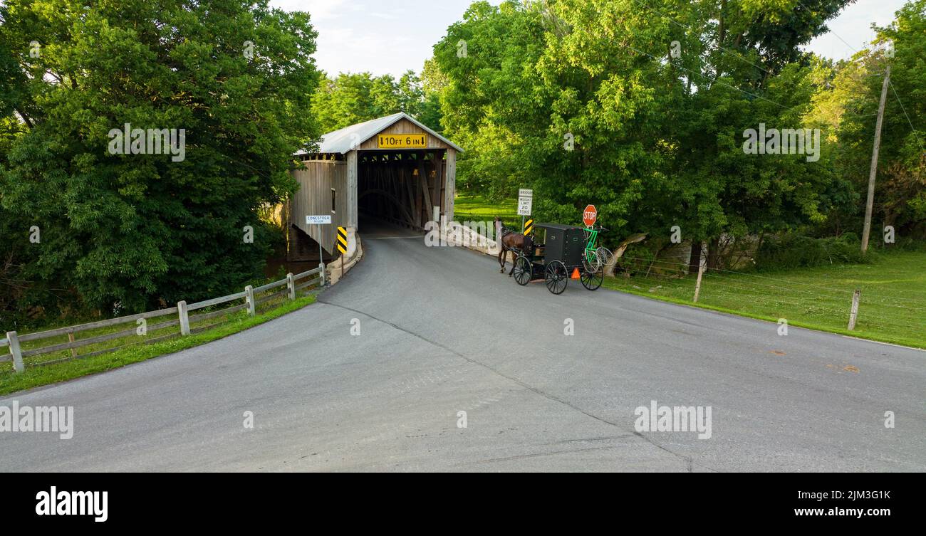 An aerial of a horse and buggy entering a covered bridge over a creek ...