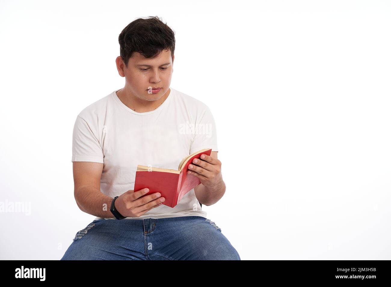 A Latin man reading a red book in a white shirt and blue jeans ...
