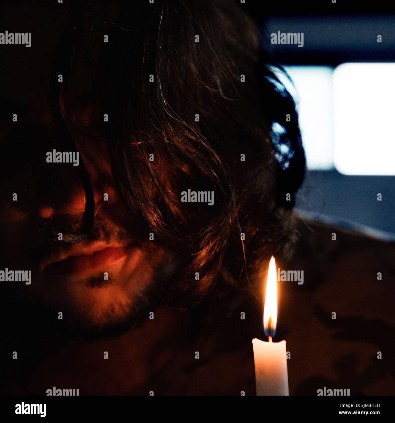 A man looks at a lit candle in the dark Stock Photo - Alamy