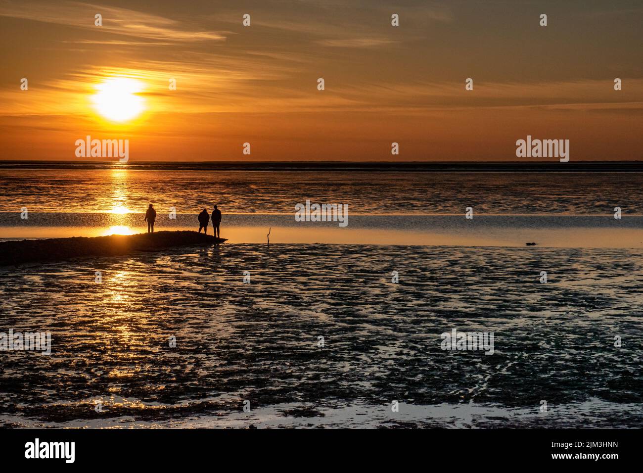 A golden sunset peeking through the clouds over the wavy waters at a ...