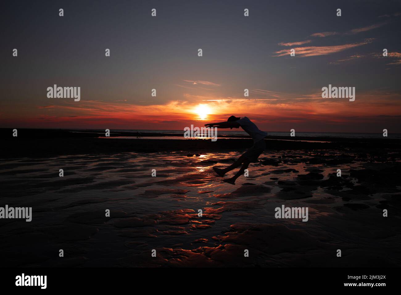A silhouette of a person jumping under a sunset sky on the Caota dune ...