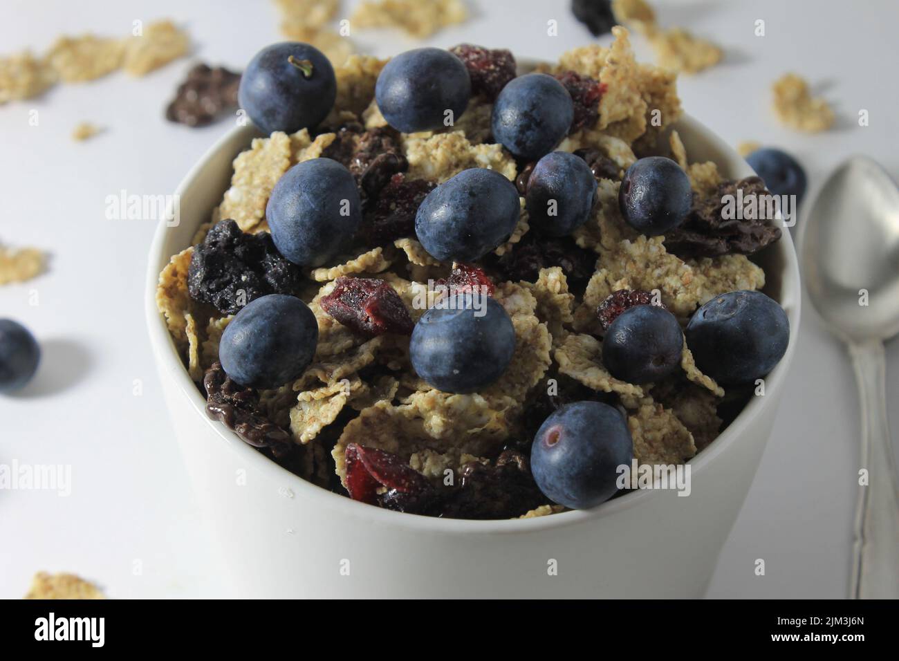 grains flakes with blueberry inside white bowl, with spoon next to it ...