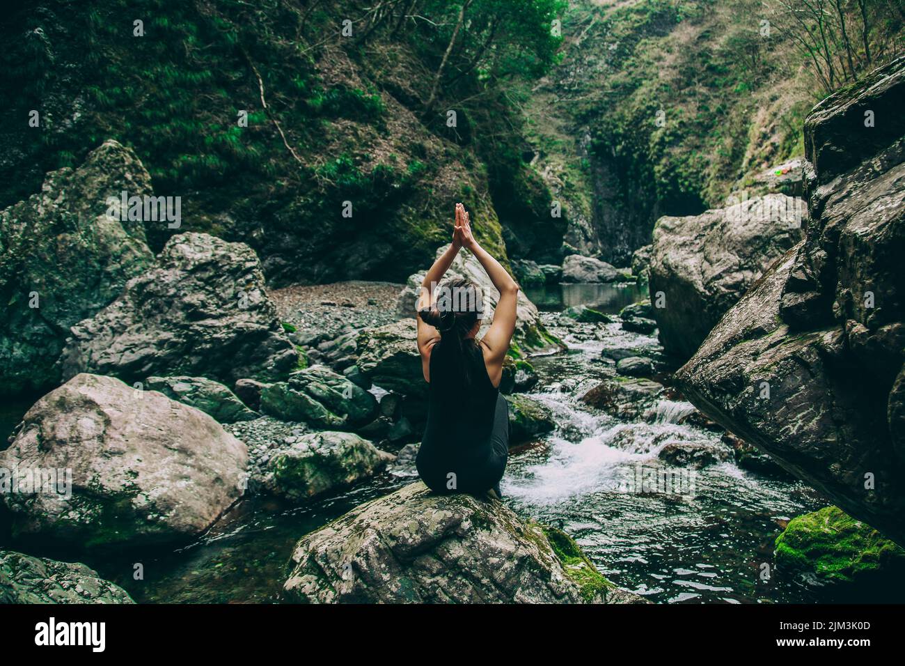 A back view of a female practicing yoga sitting on the rocks in a ...