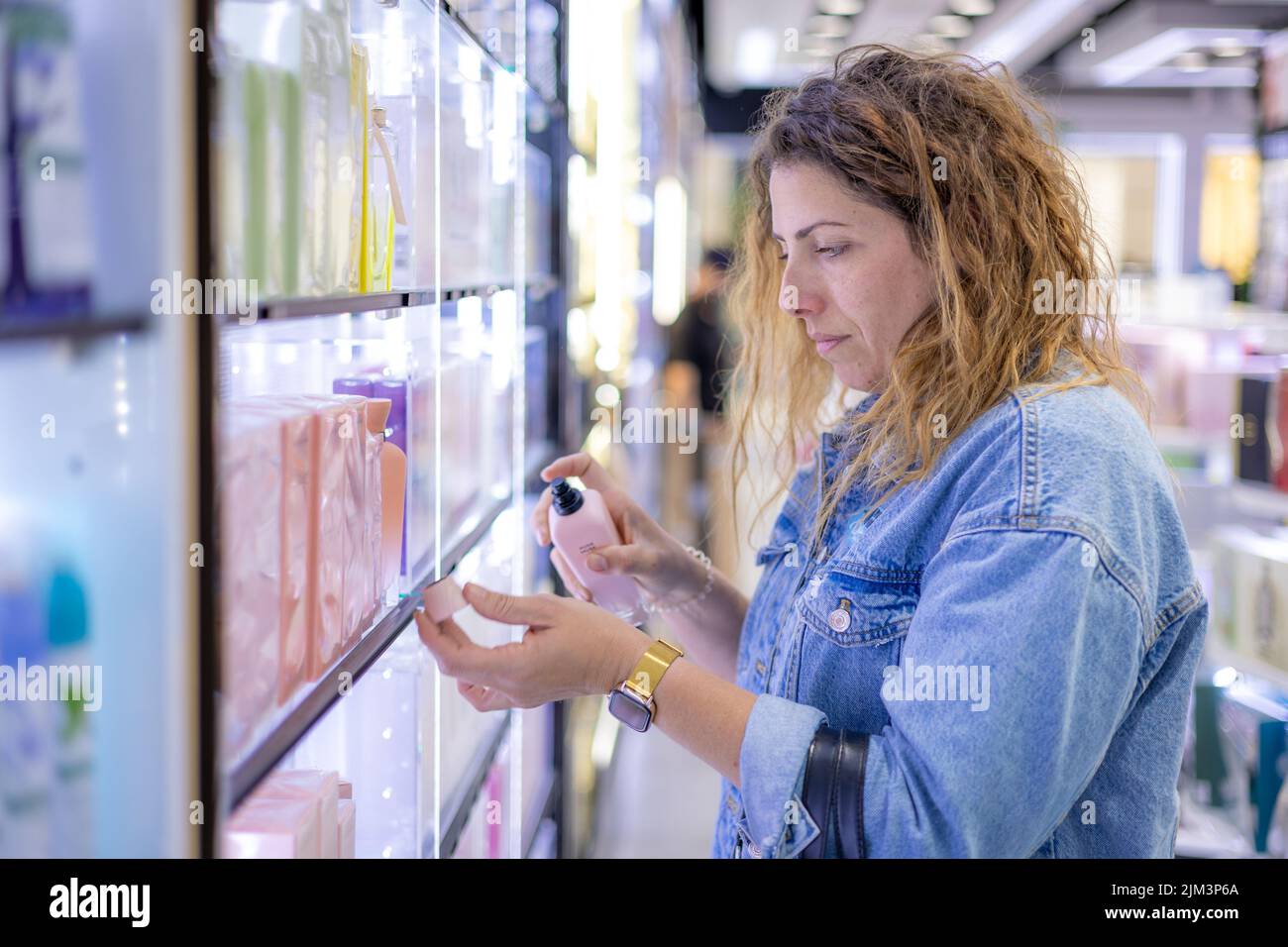 A curly haired Caucasian female checking the perfume in a perfume shop ...