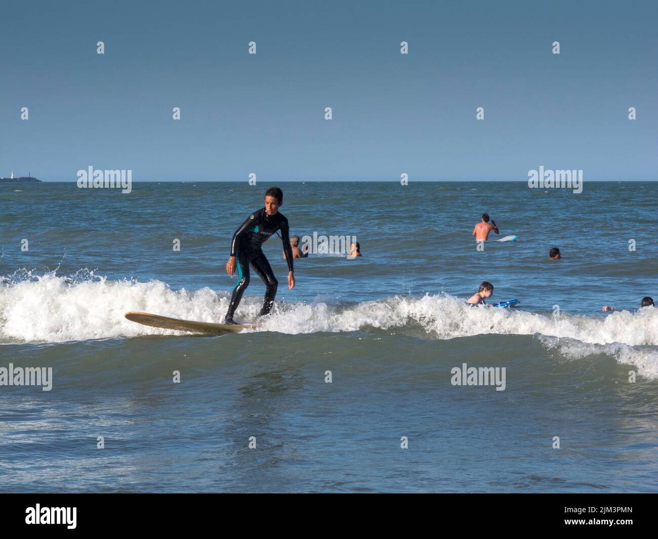 A male surfing on the water with swimmers on the beach on a sunny ...
