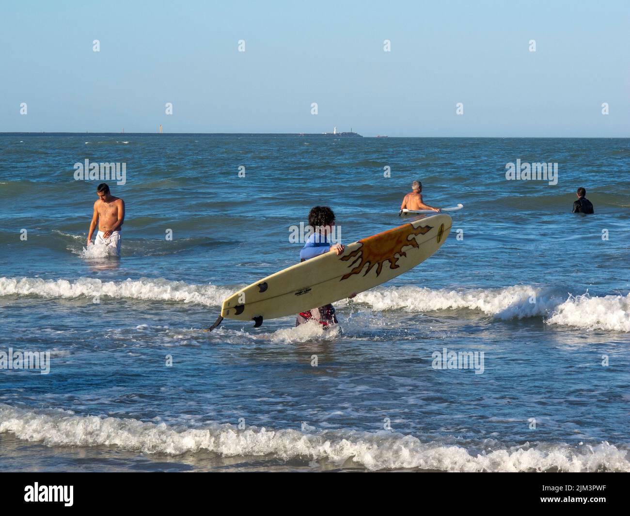 A male holding a surfing board on the water with swimmers on the beach ...