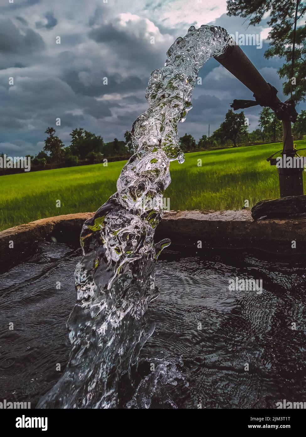 A vertical shot of water pouring out of a tube in a rural area in ...