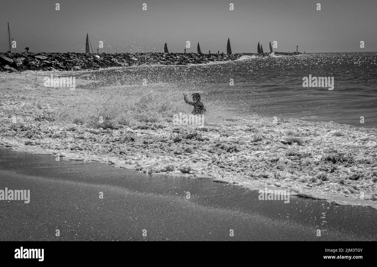 A grayscale view of a person under wave splash in The Wedge of Newport ...