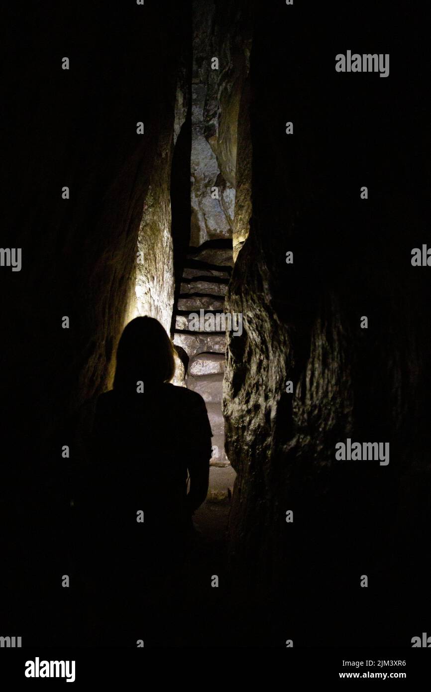 Vertical shot of a woman inside a rock cave with a lamp in Luxemburg ...