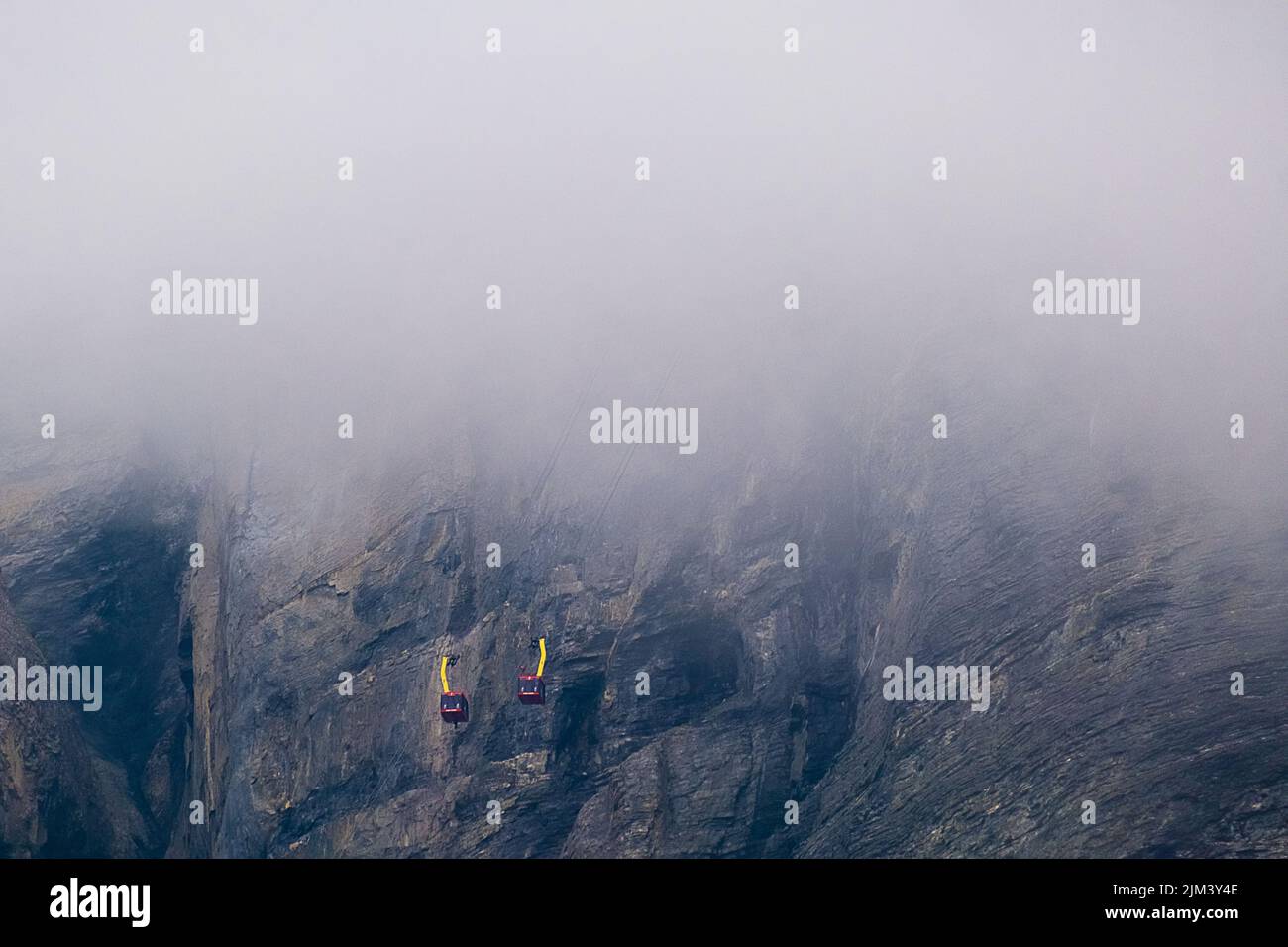 A ropeway with 2 cable cars going in front of mountains and clouds ...