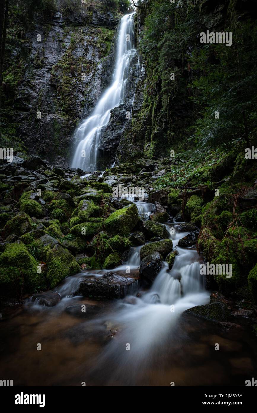 A vertical breathtaking view of a waterfall flowing through the rocks ...