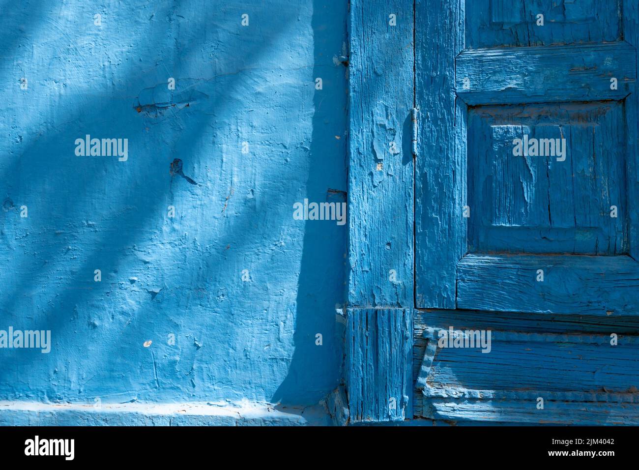 Detail of a weathered blue paint on a wooden shutter and stone wall of ...