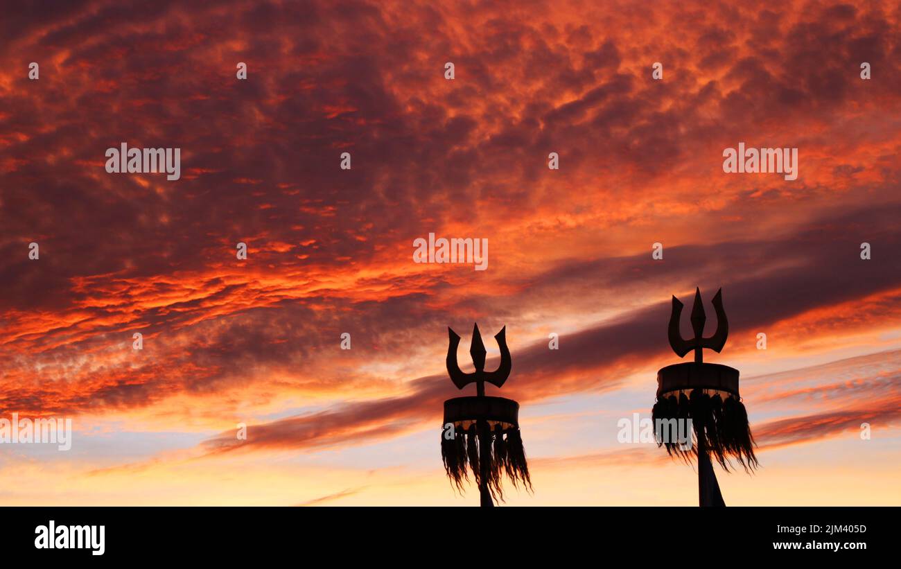 A view of Shiva Trishulas against the vibrant sunset sky with hot ...