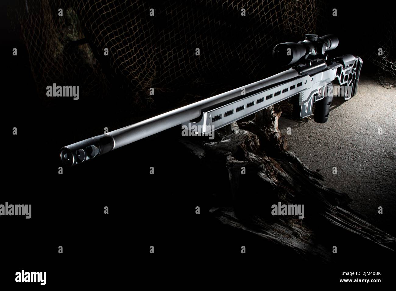 High powered rifle and scope steadied on a log with neeting behind ...