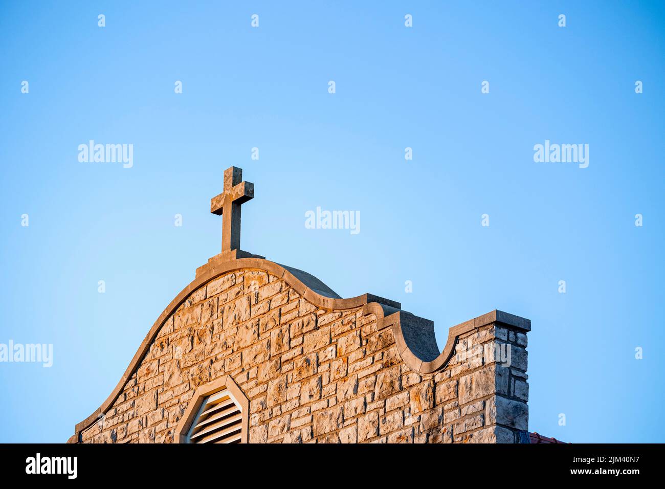 A closeup of a stone cross on the top of a building against blue cloudy ...