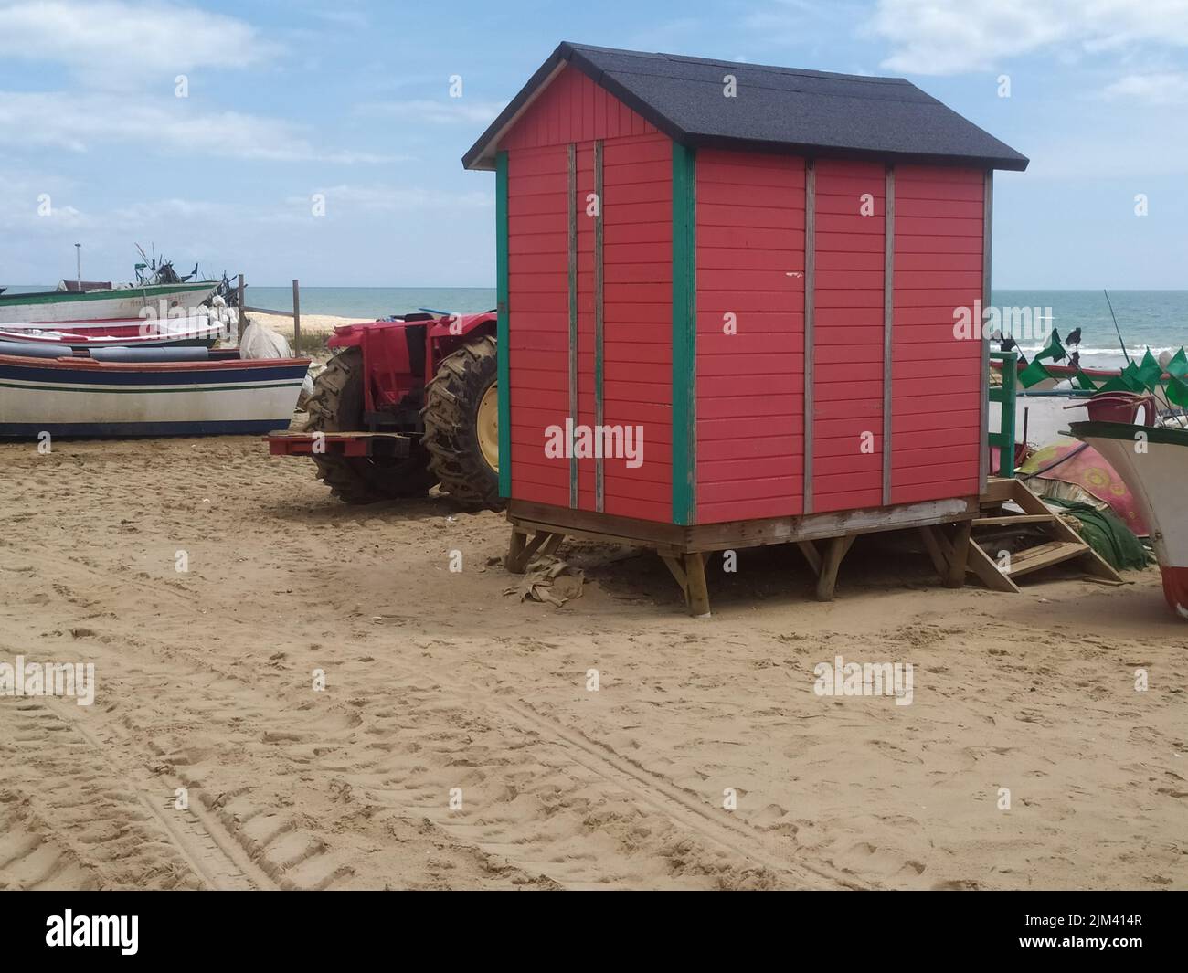 A red cabin in sandy beach near boats in background of sea Stock Photo ...