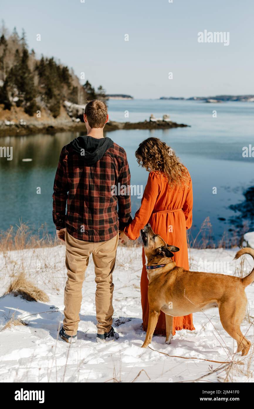 A backshot of a couple standing on the snowy ground with a doge on the ...