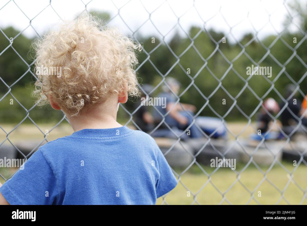A backshot of a baby boy 3 years old standing behind a grid fence in ...