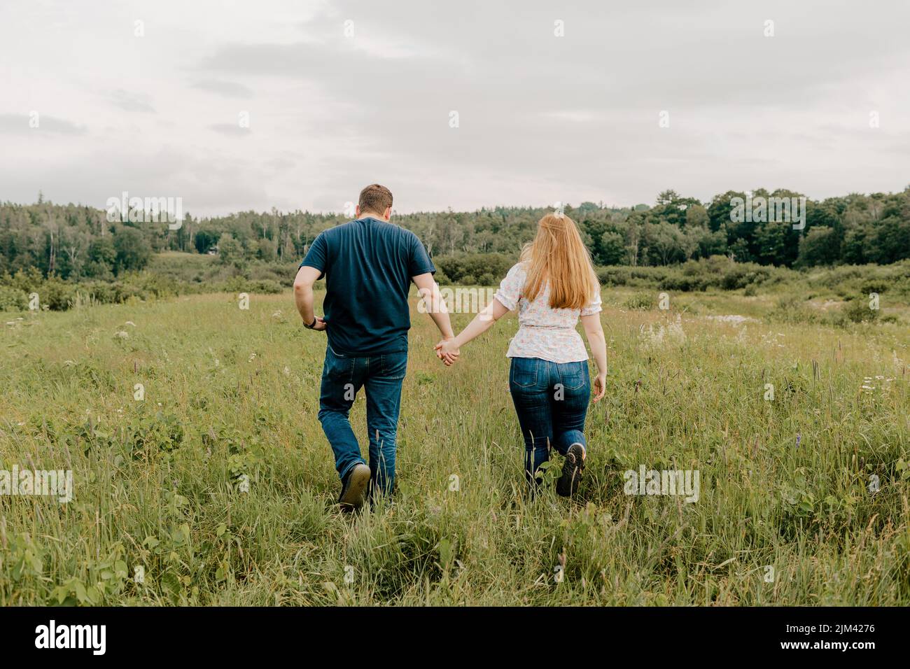 A backshot of a couple running on a green field on a sunny day against ...