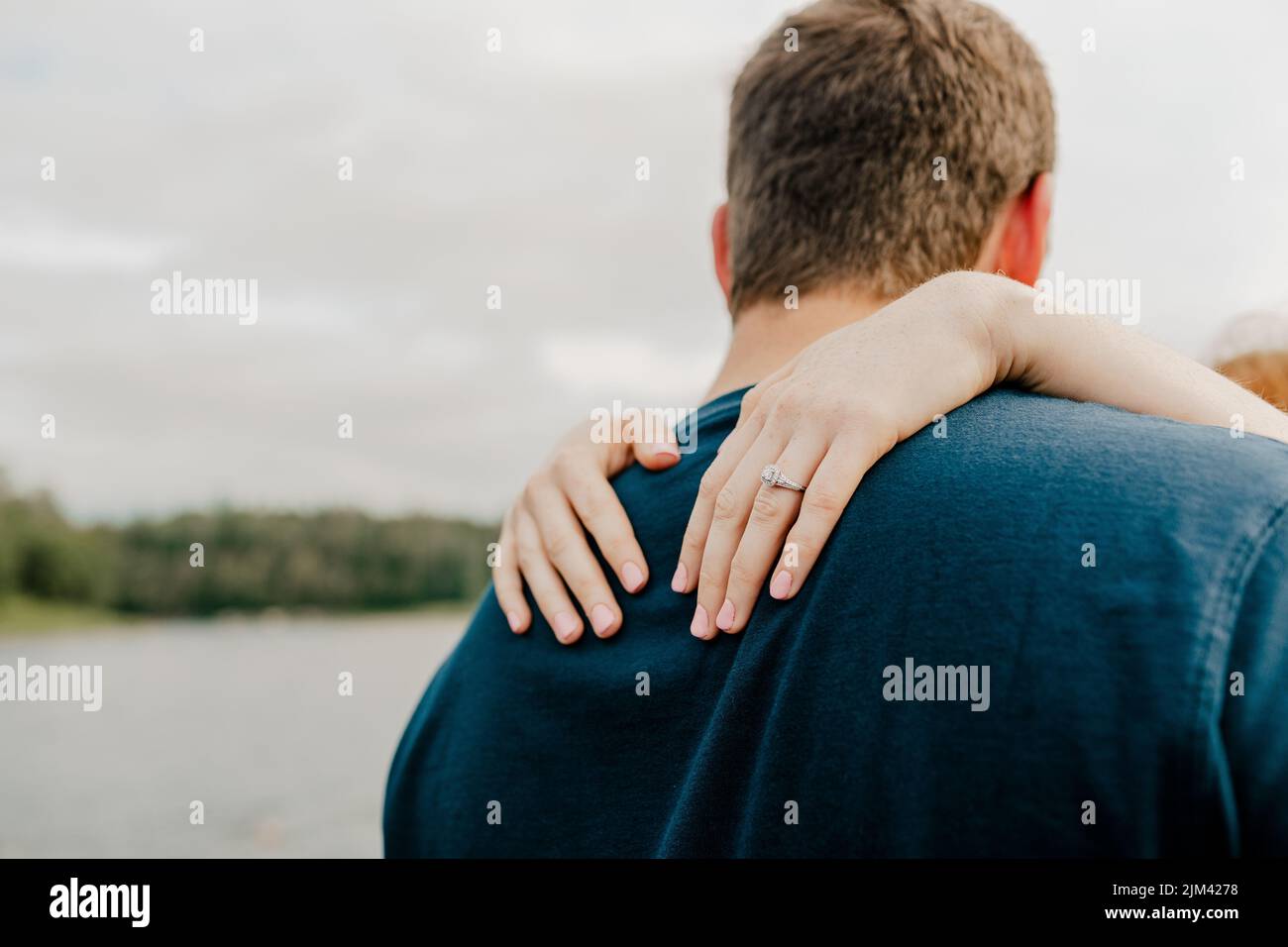 A closeup shot of the engagement ring with a beautiful couple hugging ...