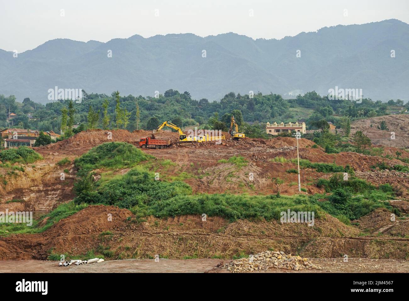 Excavator on dirt and grass hills in a village with mountains in the ...