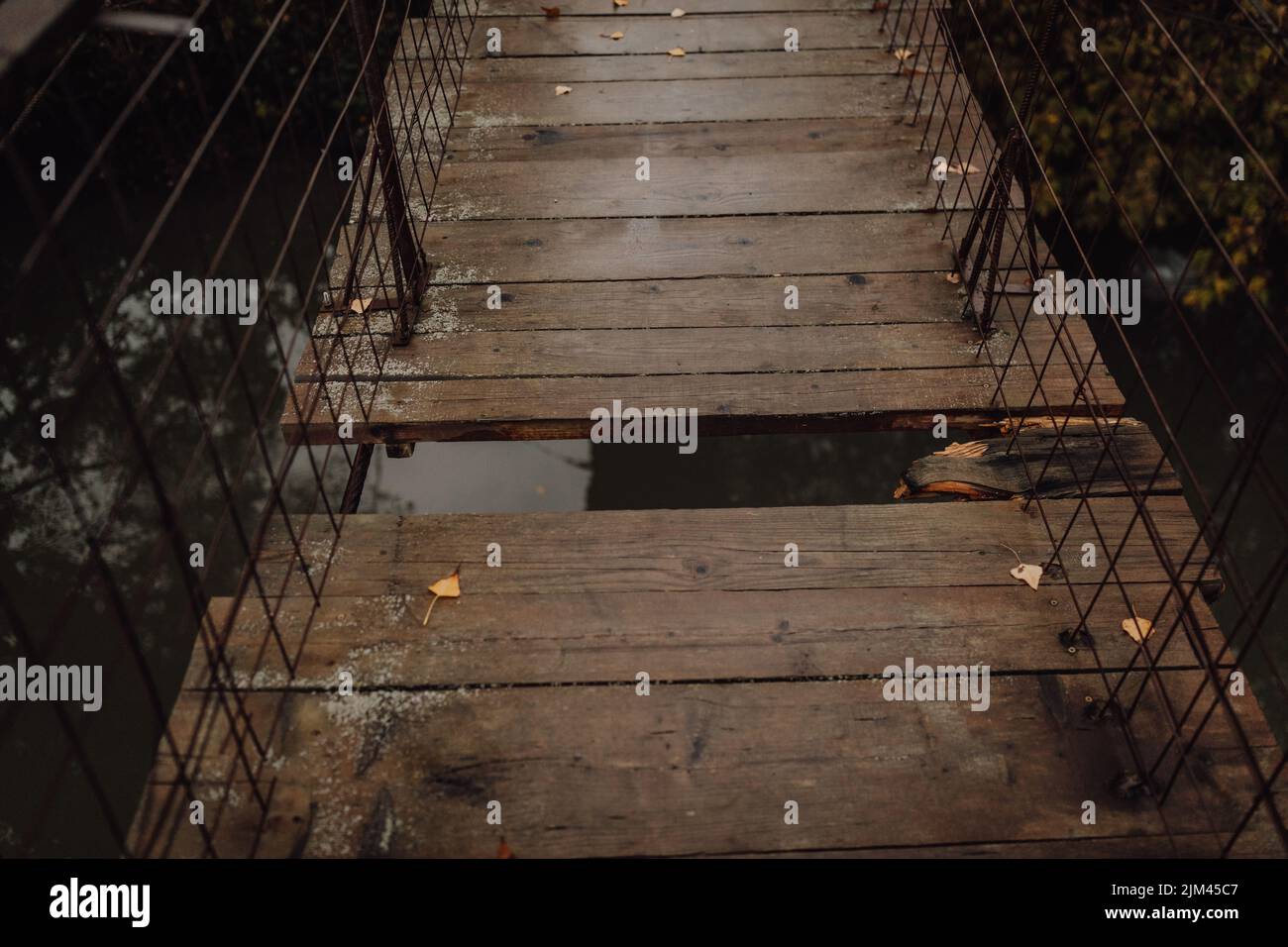A closeup of an old wooden bridge with a missing line above the river ...