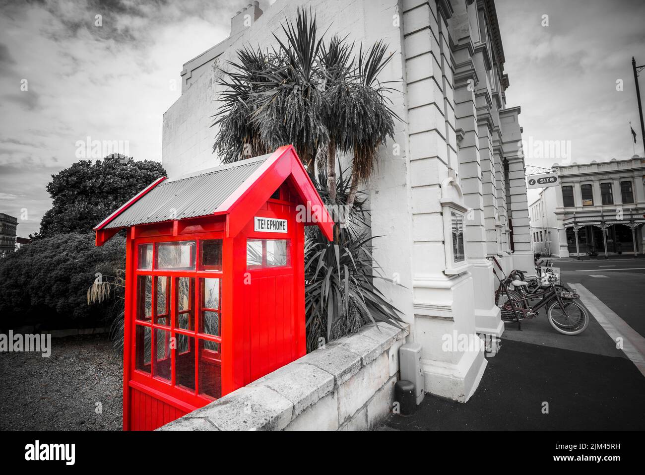 An old red telephone booth in the corner of a white building near a ...