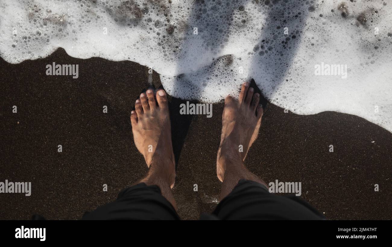 A top view of a person's feet on the beach with splashing sea waves ...
