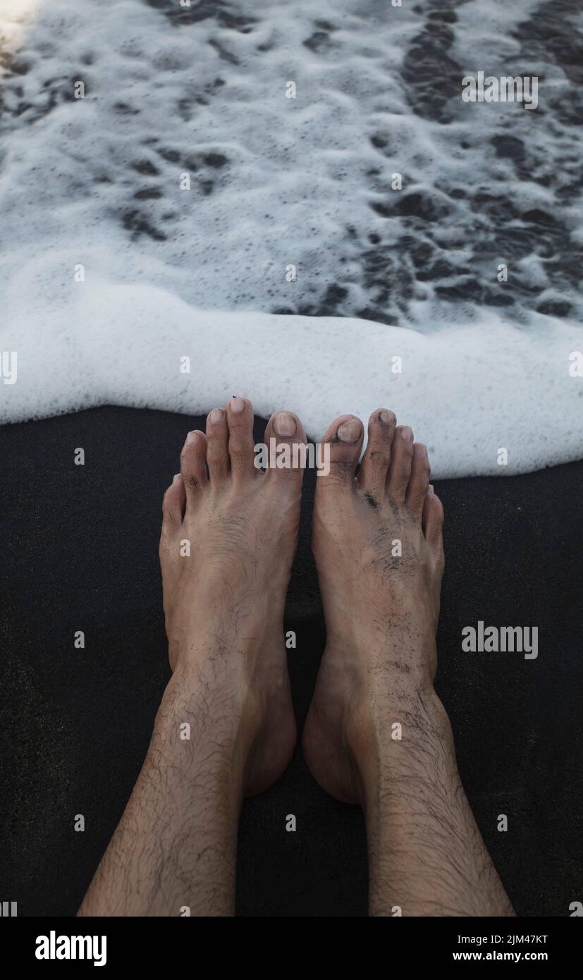 A vertical shot of a person's feet on the beach with splashing sea ...