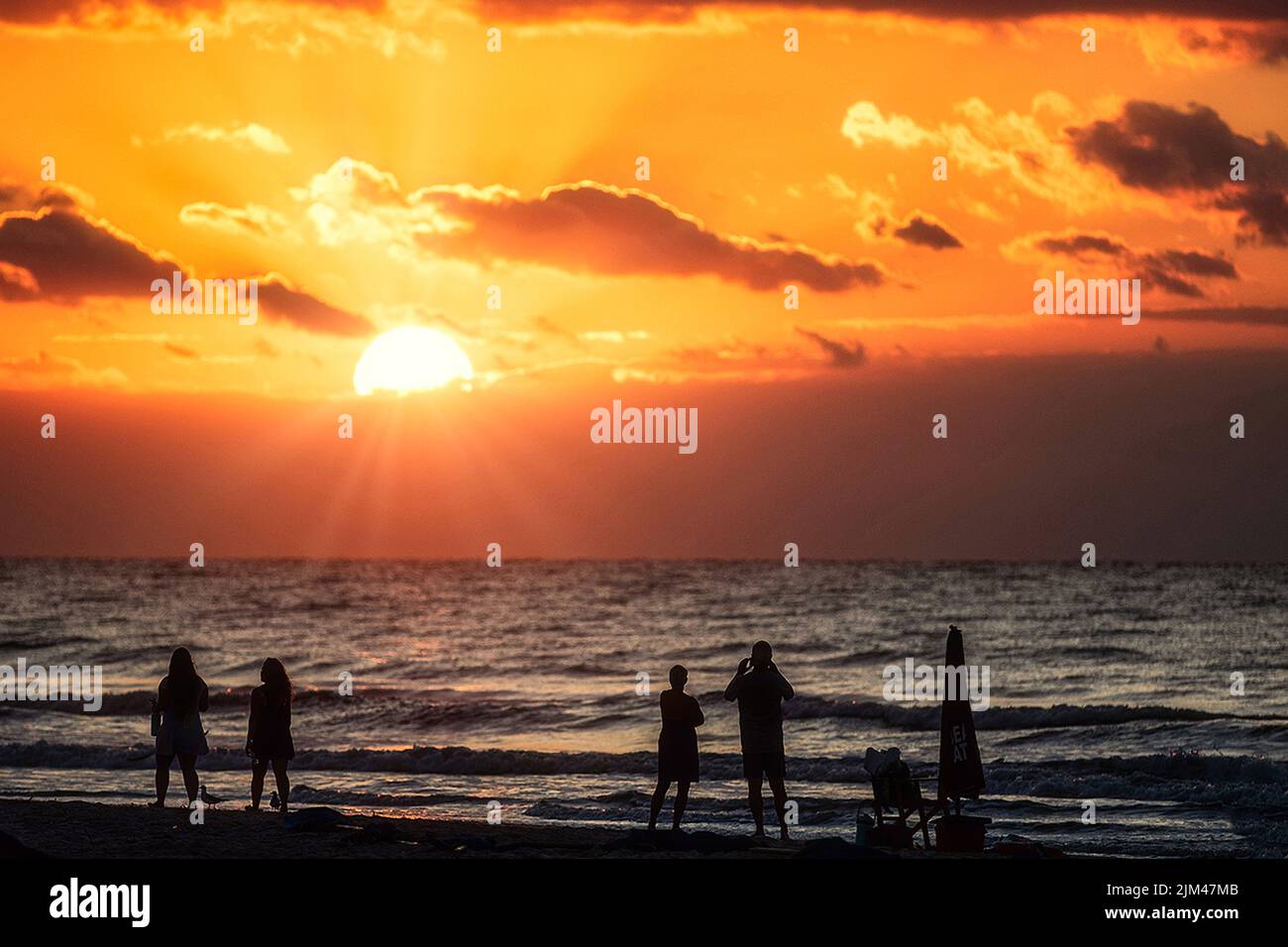 A silhouette of people looking at the beautiful sunset at the beach ...